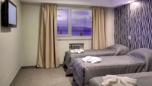 Quarto de hotel com duas camas, televisão, janela com cortinas e radiador.