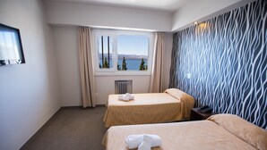 Quarto de hotel com duas camas, janela com vista para montanhas e árvores, radiador e parede com padrão.