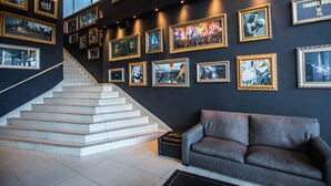 Uma escadaria com degraus brancos que leva a um patamar, um sofá cinza e uma parede decorada com fotografias emolduradas.