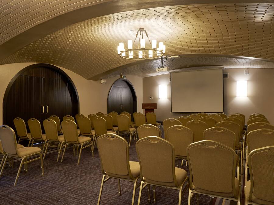 Uma sala de conferências com fileiras de cadeiras, uma tela de projetor e um candelabro.