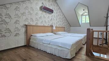 Quarto com teto inclinado, estrutura de cama de madeira, colcha branca e ar-condicionado fixado na parede.
