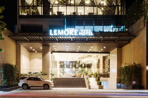 Entrada do Hotel Lemore com design moderno, um carro estacionado em frente e uma escadaria que leva à entrada.