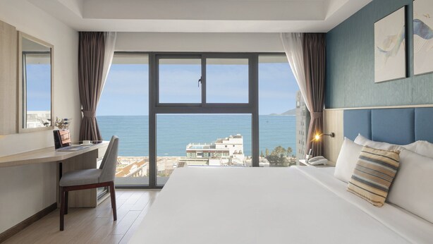 Quarto de hotel com uma cama grande, uma escrivaninha e vista para o mar.