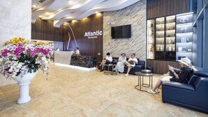 Uma área de recepção de hotel com um balcão de mármore, um arranjo floral grande e uma área de estar com sofás.