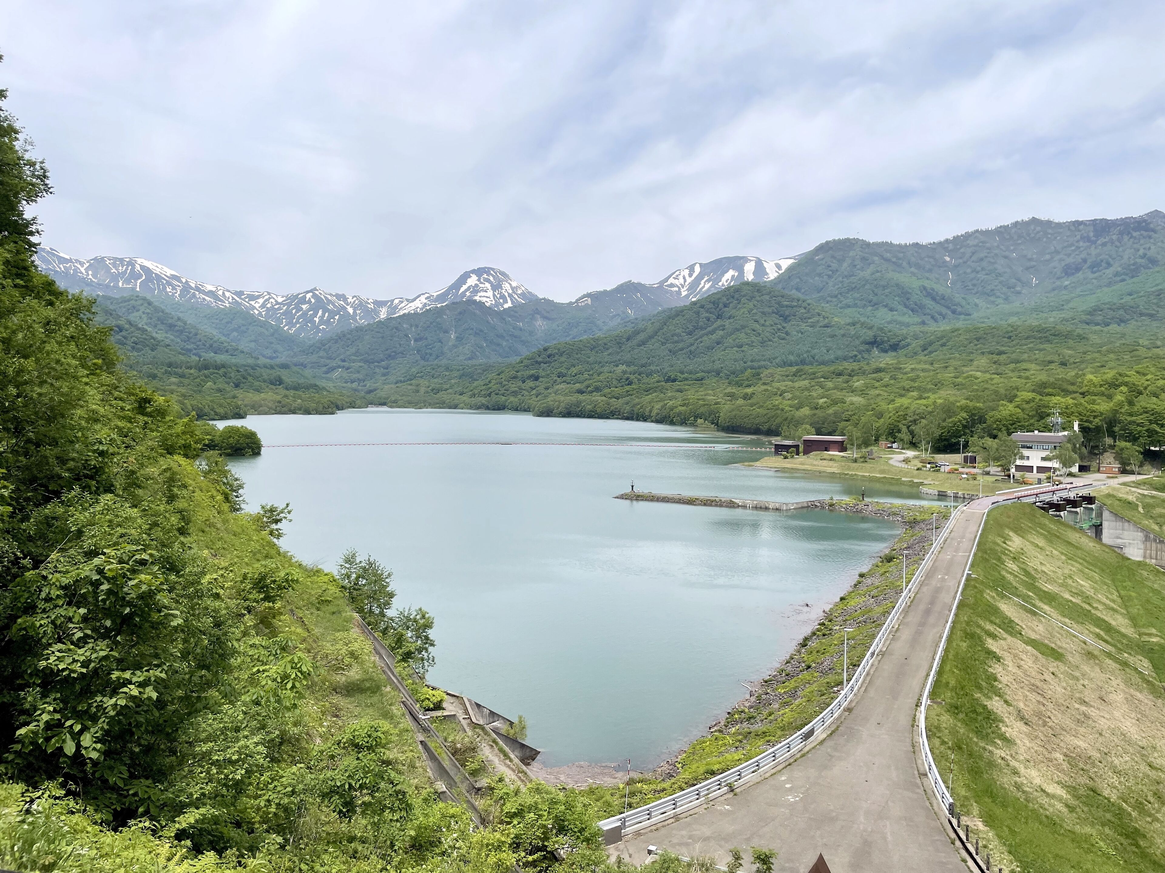 Um lago rodeado por montanhas, uma estrada e alguns edifícios.