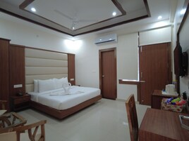 Quarto de hotel moderno com uma cama grande, painel de cabeceira em madeira, ventilador de teto, ar condicionado, escrivaninha de madeira e televisão na parede.