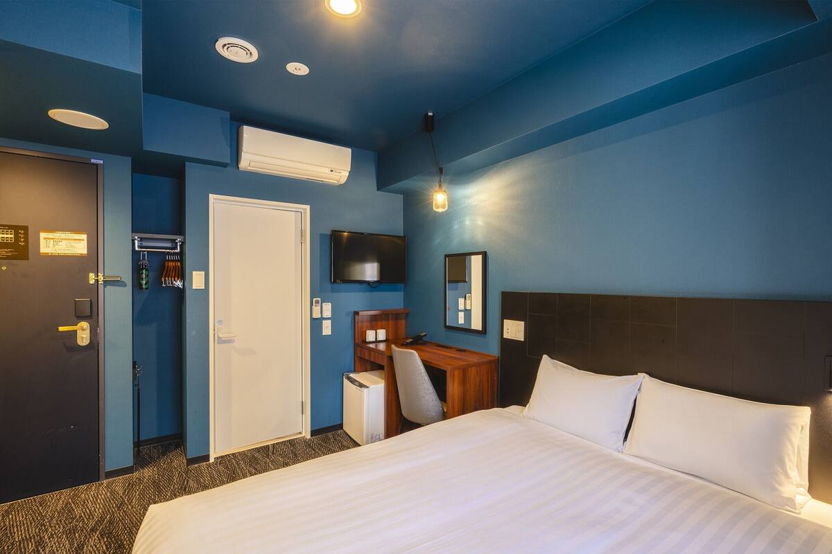 Quarto de hotel com uma cama grande, uma escrivaninha com cadeira, televisão de tela plana e porta com tranca por cartão.