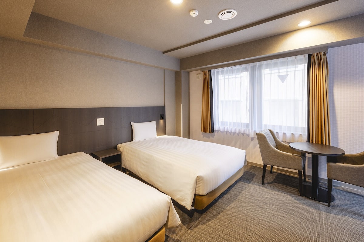 Quarto de hotel com duas camas, uma escrivaninha e uma cadeira.