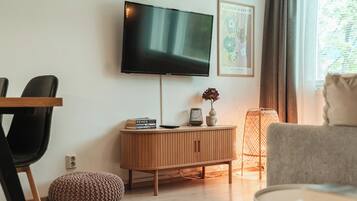 Uma sala de estar moderna com uma TV de tela plana na parede, um armário de madeira, um banquinho redondo e uma moldura com um quadro na parede.