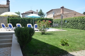 Um jardim com cadeiras de descanso e guarda-sóis, edifícios de pedra e um gramado bem cuidado.