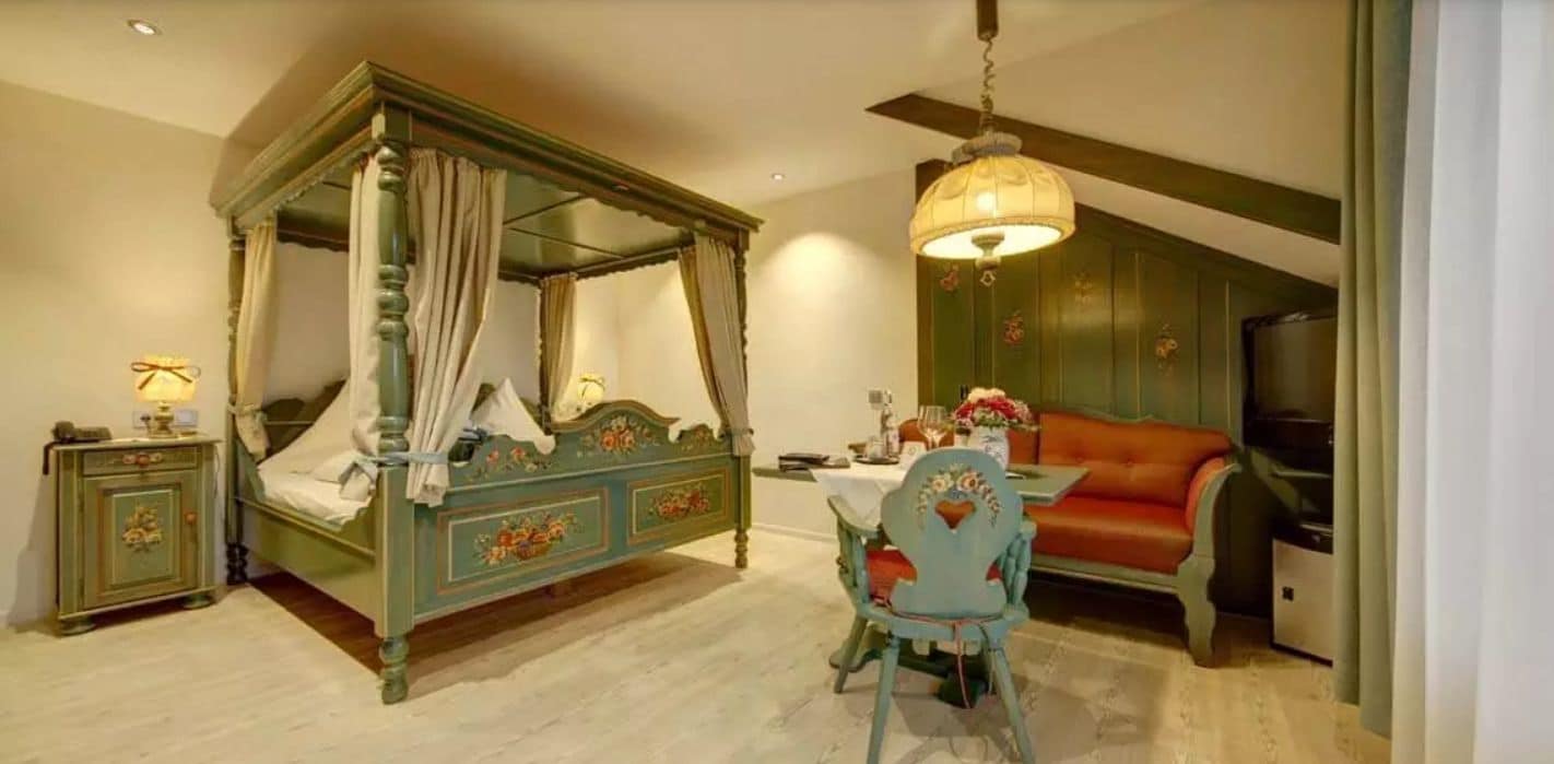 Quarto com cama de dossel, uma mesinha com um vaso e um sofá vermelho.