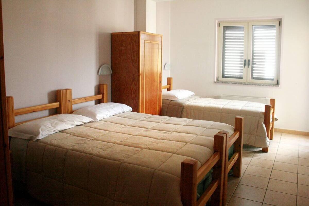 Quarto com duas camas de madeira, um guarda-roupa e uma janela com persianas.