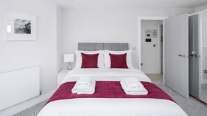 Quarto de hotel moderno com cama bem arrumada, mesa de cabeceira com abajur e porta que dá para um banheiro.