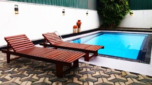Piscina com duas espreguiçadeiras de madeira e piso estampado.