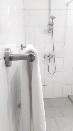 Um banheiro com porta-toalhas, chuveiro e paredes revestidas com azulejos.