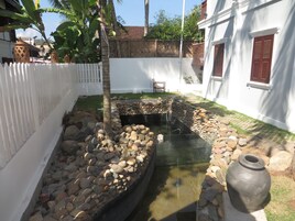 Um pátio com um pequeno lago, paredes brancas e cerca branca.