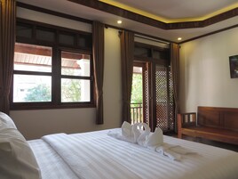 Quarto de hotel com uma cama grande, cabeceira de madeira, um banquinho de madeira e uma janela com cortinas.