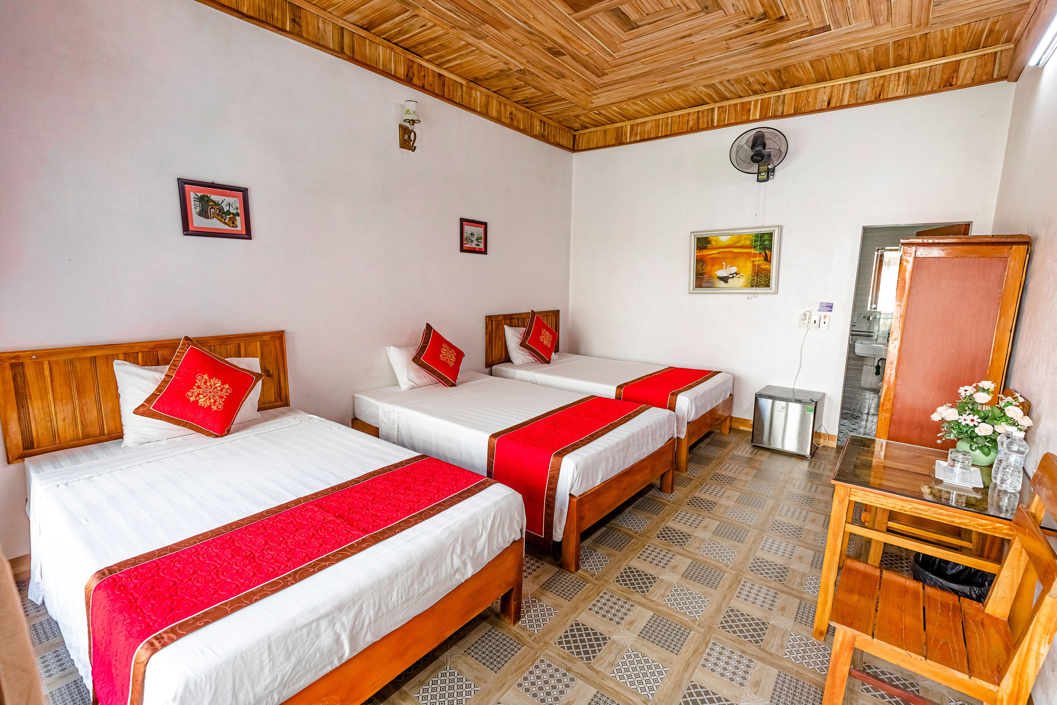 Quarto de hotel com três camas, cabeceiras de madeira e uma mesa de jantar com cadeiras.