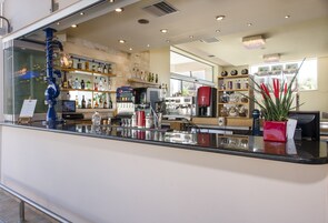 Uma área de bar com balcão, prateleiras com garrafas, uma máquina de café e um dispensador de bebidas vermelho.