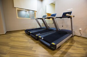 Um quarto com quatro esteiras de corrida alinhadas, uma janela e piso de madeira.