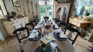 Uma sala de jantar com uma mesa comprida posta para refeição, rodeada de cadeiras.