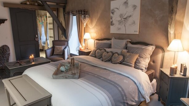 Quarto com cama, mesas de cabeceira, um banco e uma obra de arte na parede.