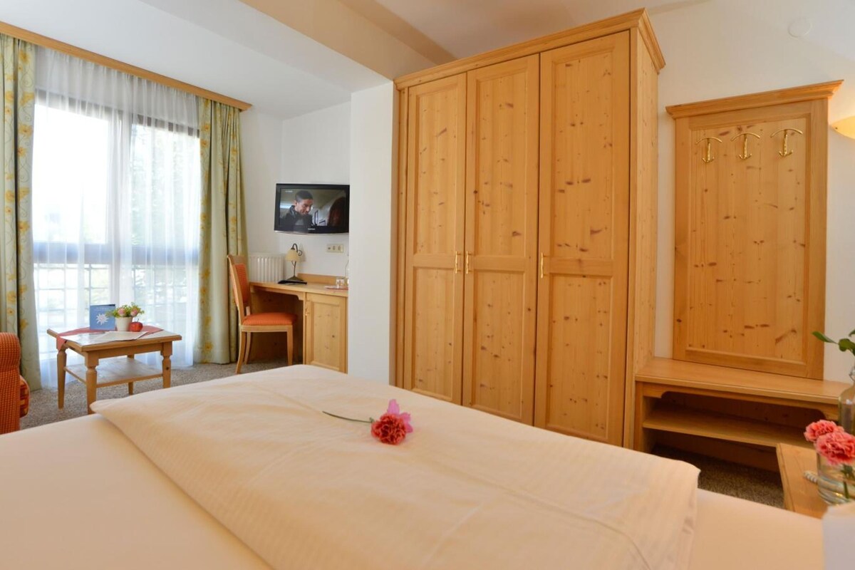 Quarto de hotel com cama, escrivaninha, cadeira, televisão e armários de madeira.