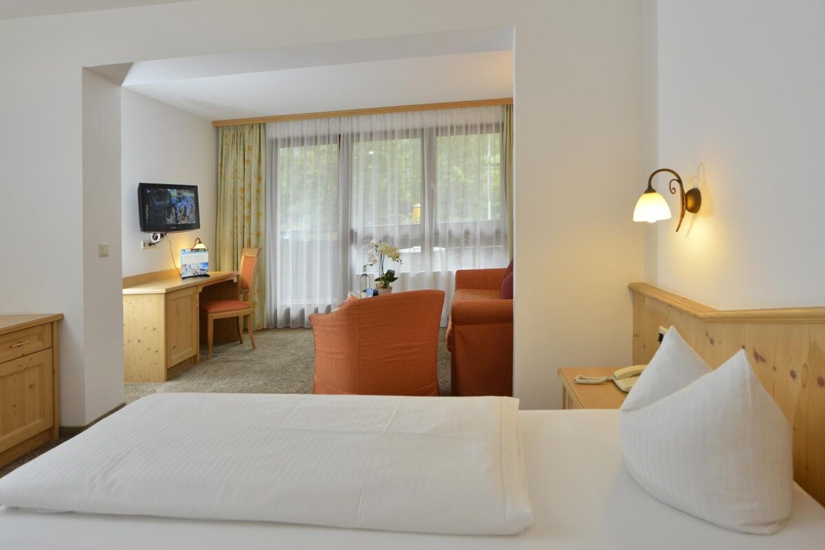 Quarto de hotel com cama, escrivaninha com computador, televisão e luminária.