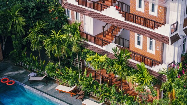Hotel de vários andares com piscina, palmeiras e fachada de tijolo.