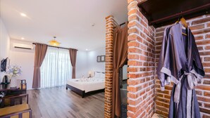 Quarto de hotel com cama, escrivaninha com cadeira, roupão pendurado e parede de tijolos.