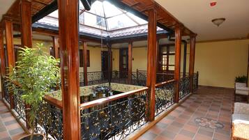 Amplo espaço interno com teto alto, colunas de madeira, claraboia de vidro e piso de azulejos.
