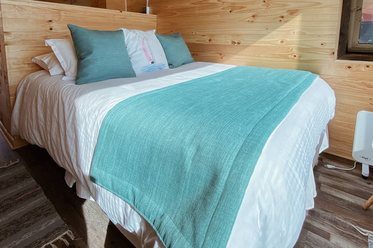 Quarto de cabana de madeira com uma cama, travesseiros, um cobertor, um quadro na parede e uma tomada.
