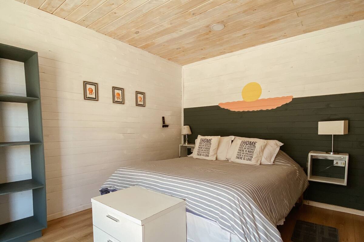 Um quarto com cama, mesa de cabeceira, cômoda e estante.