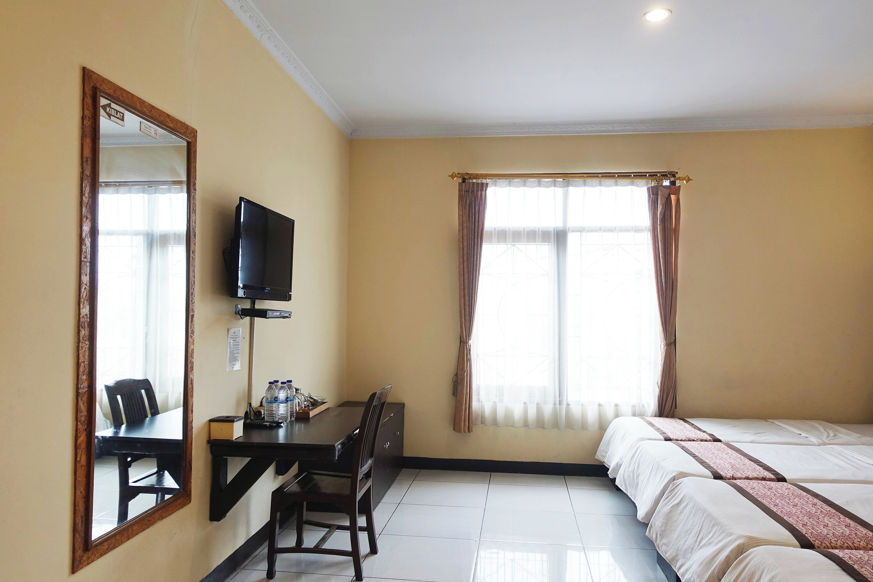 Quarto de hotel com cama, escrivaninha, cadeira, televisão e janela com cortinas.