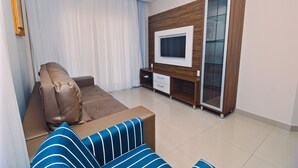 Uma sala moderna com um sofá de couro marrom, um banquinho azul listrado, um rack de madeira com uma TV e um aparador de vidro.