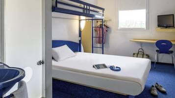 Quarto de hotel com beliche, escrivaninha com computador, janela e banheiro com pia e espelho.
