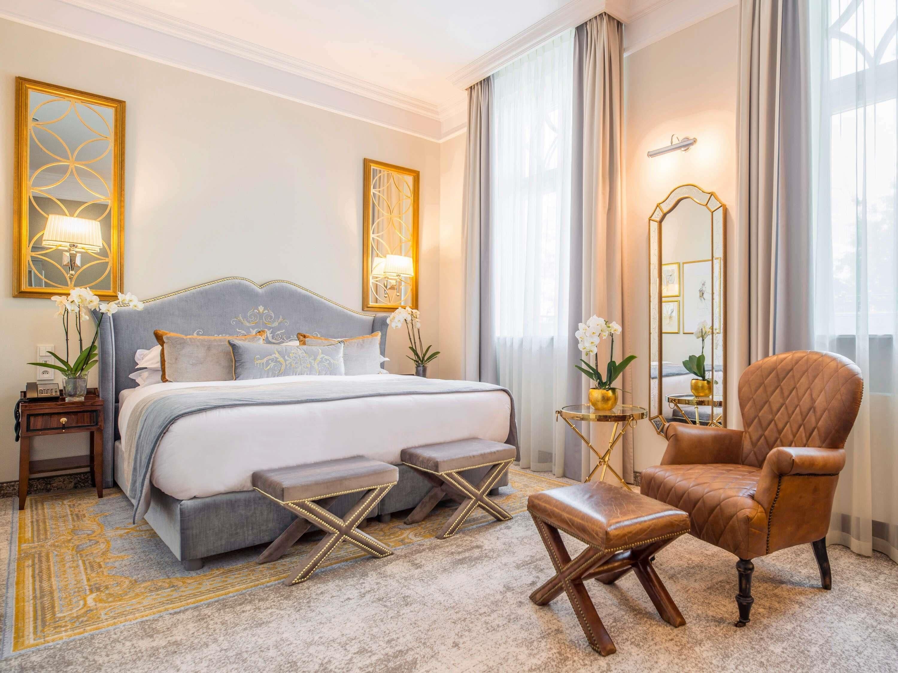 Quarto de hotel com cama, cadeira, mesinha e espelho.