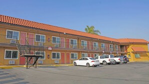Um motel com vários andares, teto de telhas vermelhas, diversas varandas e estacionamento com vários carros.