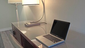Quarto de hotel moderno com escrivaninha de vidro, um laptop, uma lâmpada e uma TV de tela plana.