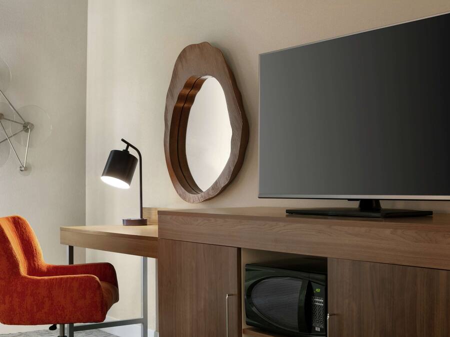 Quarto moderno com escrivaninha de madeira, televisão, televisor antigo, cadeira vermelha e luminária fixa na parede.