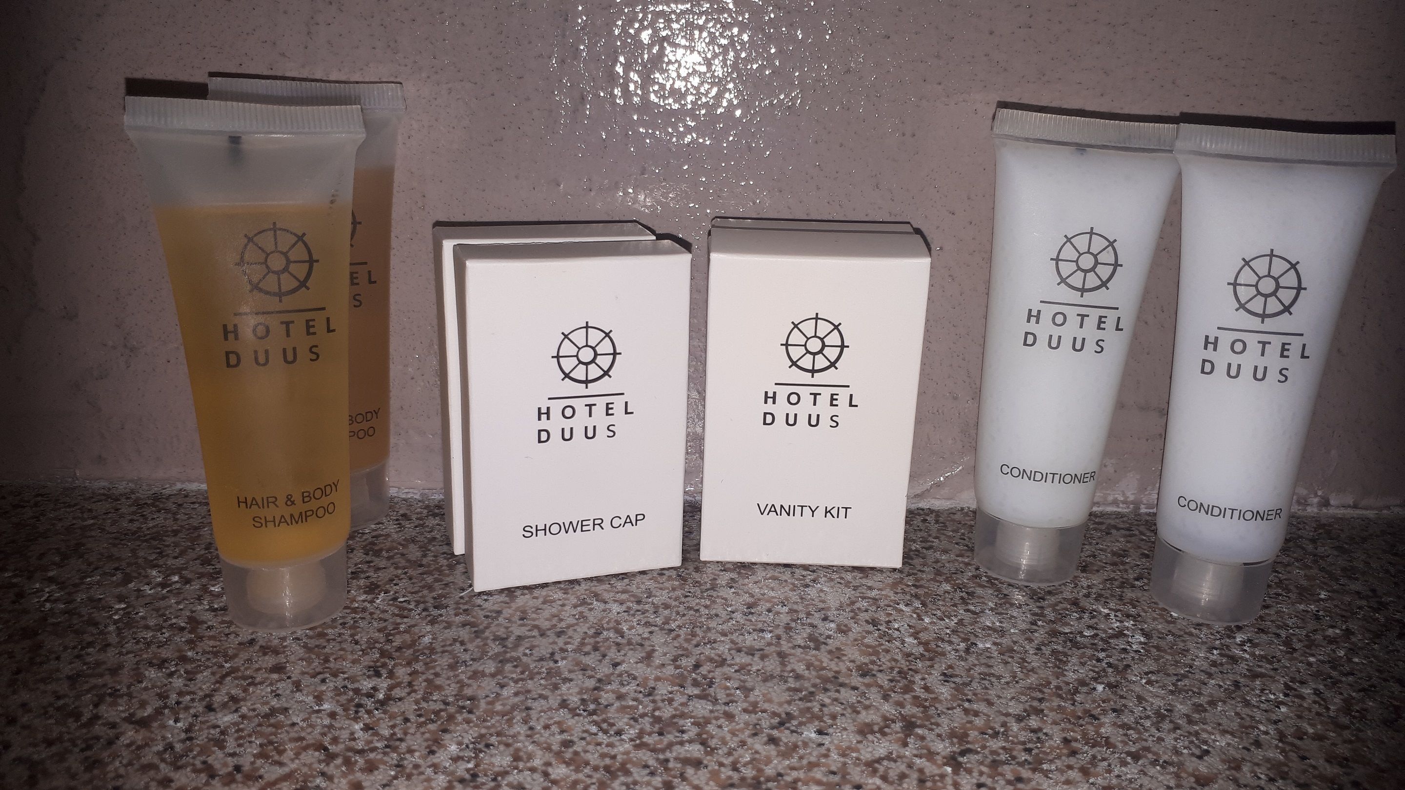 Exposição de produtos do Hotel Duus, incluindo shampoo e condicionador para cabelo e corpo, touca de banho e kit de higiene.