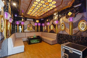 Um quarto luxuoso com um amplo sofá de canto, um pequeno bar e um teto com luminárias hexagonais.