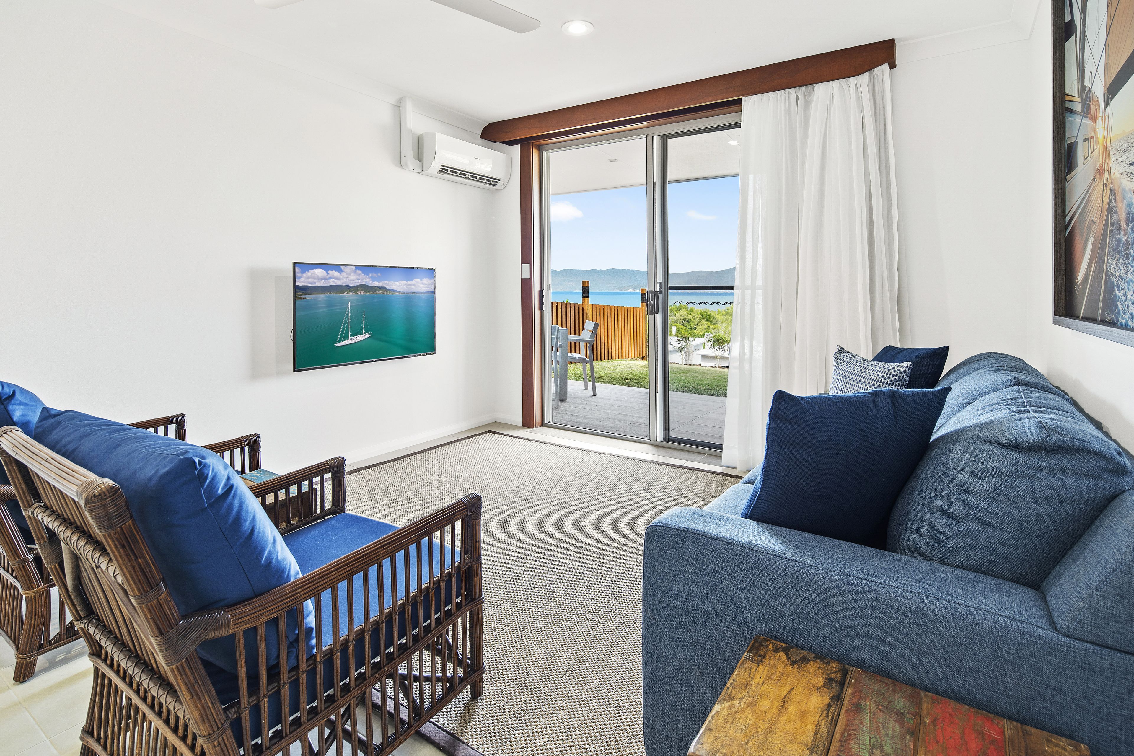 Sala de estar com vista para um corpo d'água, uma cadeira de madeira, um sofá azul e um quadro na parede.