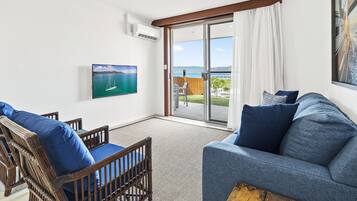 Sala de estar com vista para um corpo d'água, uma cadeira de madeira, um sofá azul e um quadro na parede.