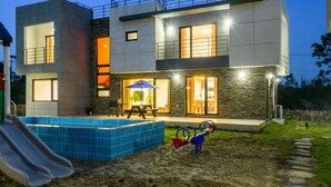 Uma casa moderna com dois andares, piscina, escorrega e área de estar externa.