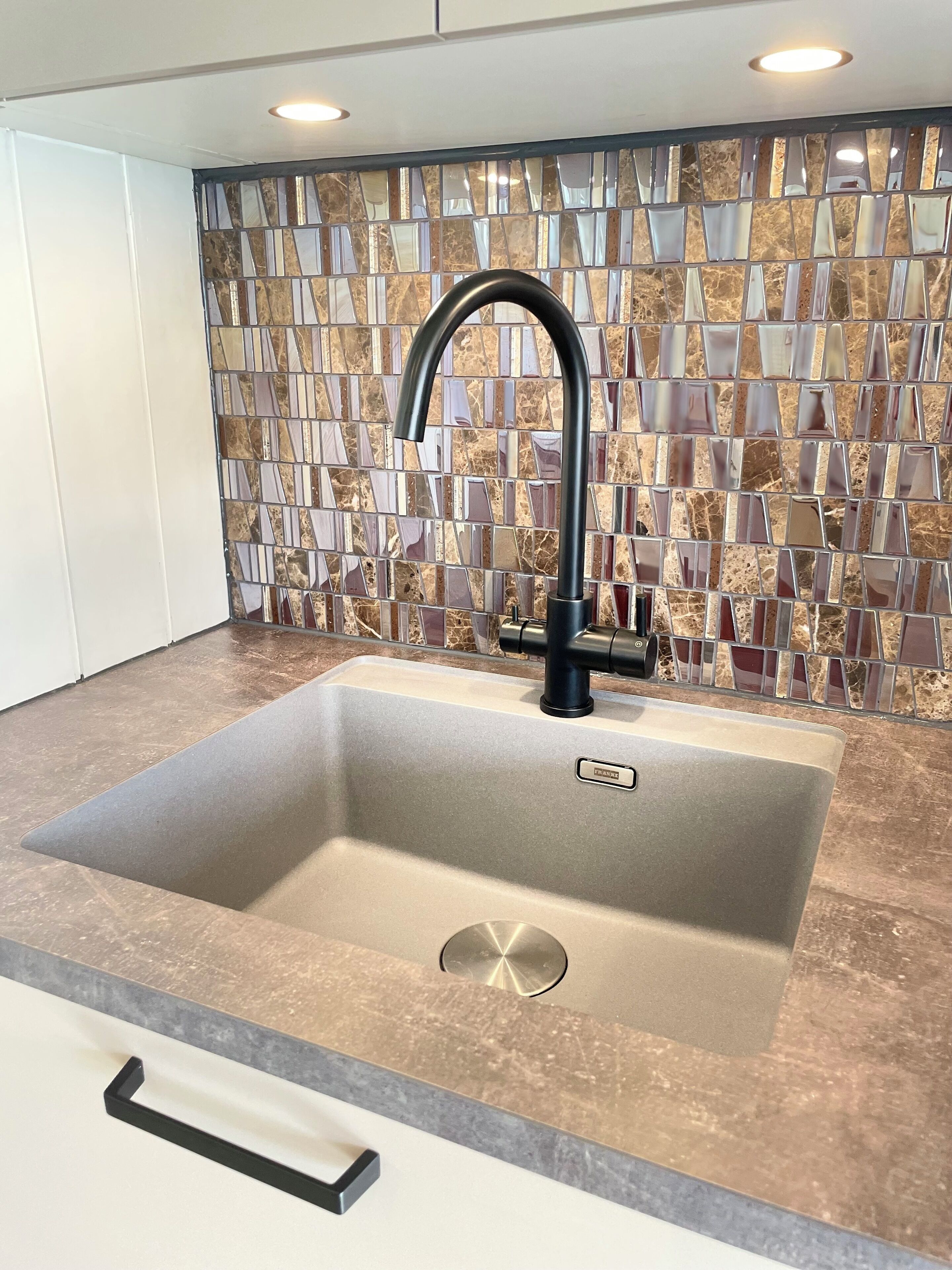 Uma cozinha com pia moderna, painel decorativo com mosaicos e bancada.