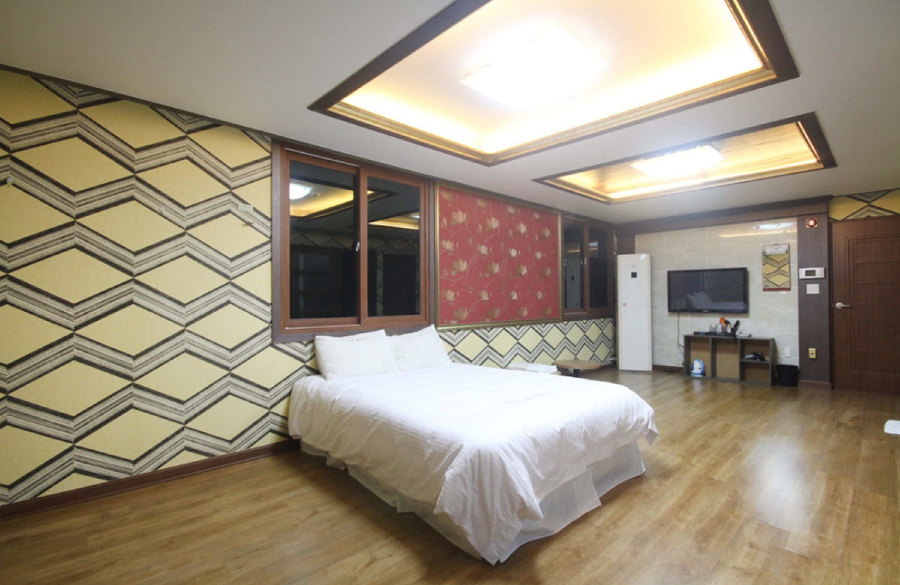 Quarto com cama, piso de madeira, papel de parede estampado, televisão e frigorífico.