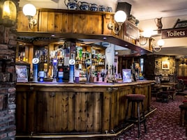 Uma área de bar com balcão de madeira, várias torneiras de cerveja e uma placa indicando a localização dos sanitários.