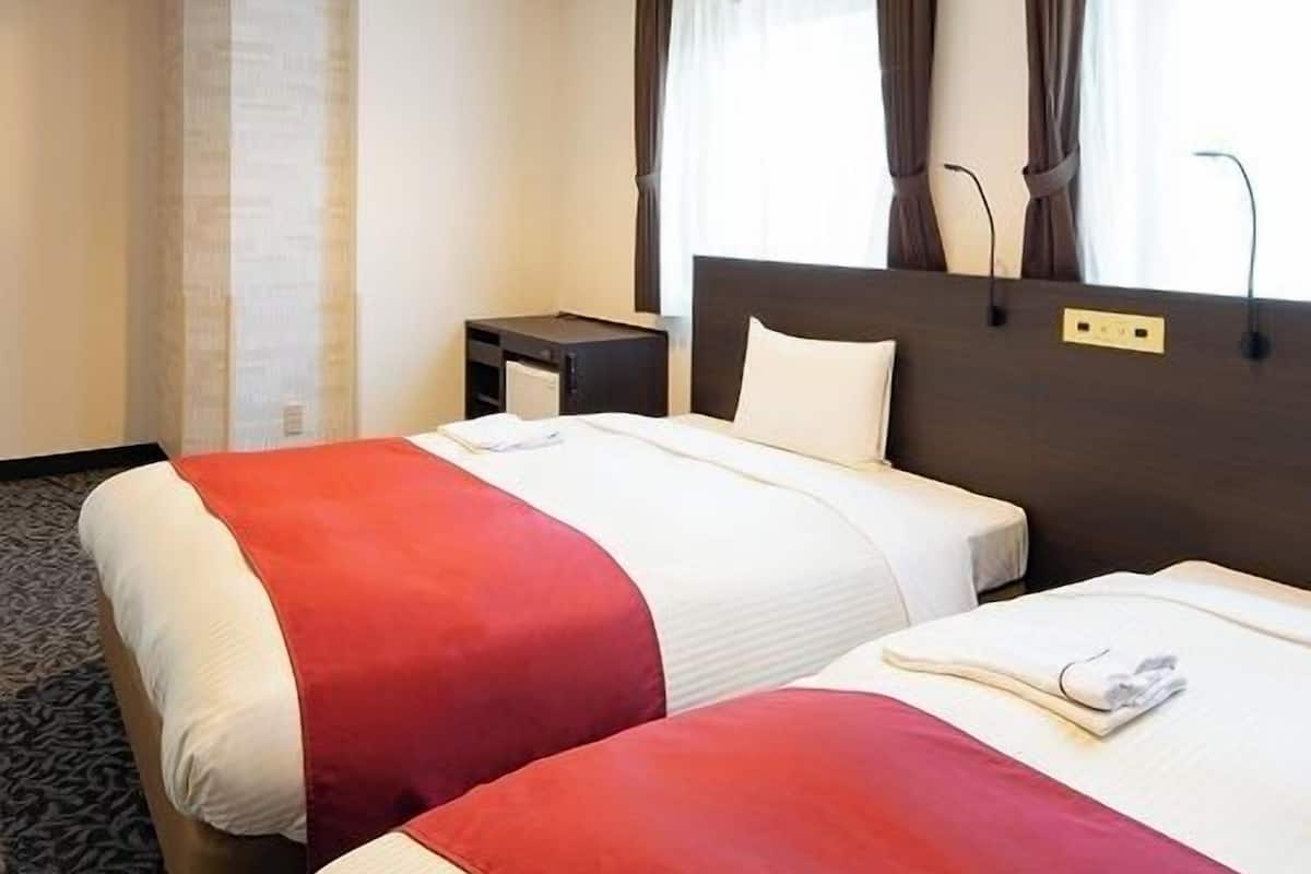 Quarto de hotel com duas camas, uma mesa de cabeceira, um abajur e uma janela com cortinas.
