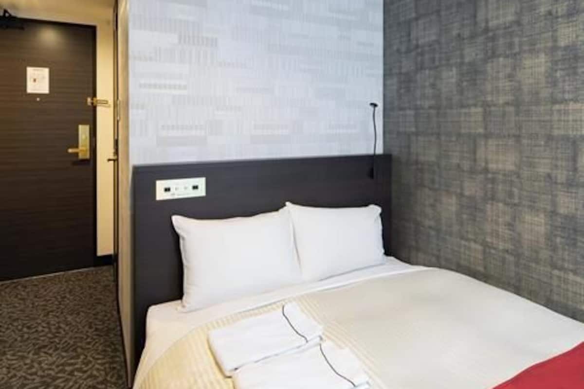 Quarto de hotel com uma cama, cabeceira escura, parede de destaque vermelha e carpete estampado.